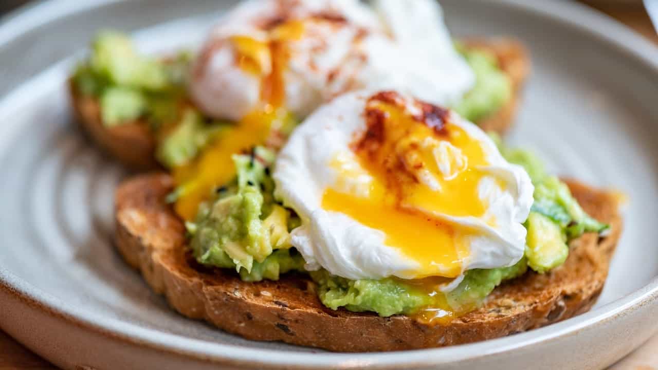 Tostada de pan integral con aguacate, huevos escalfados y condimento ...